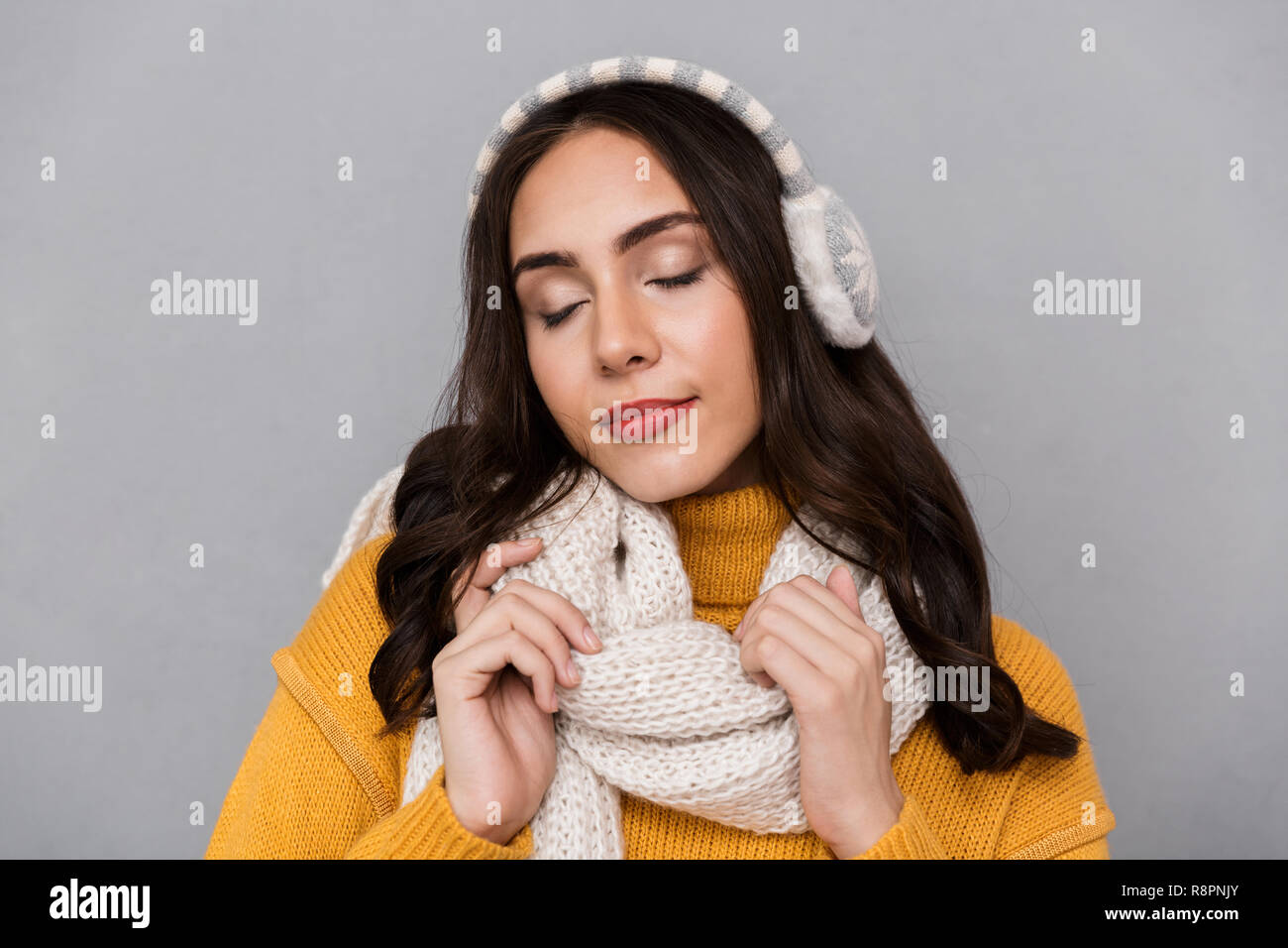Portrait of cute woman wearing ear muffs and scarf smiling and touching ...