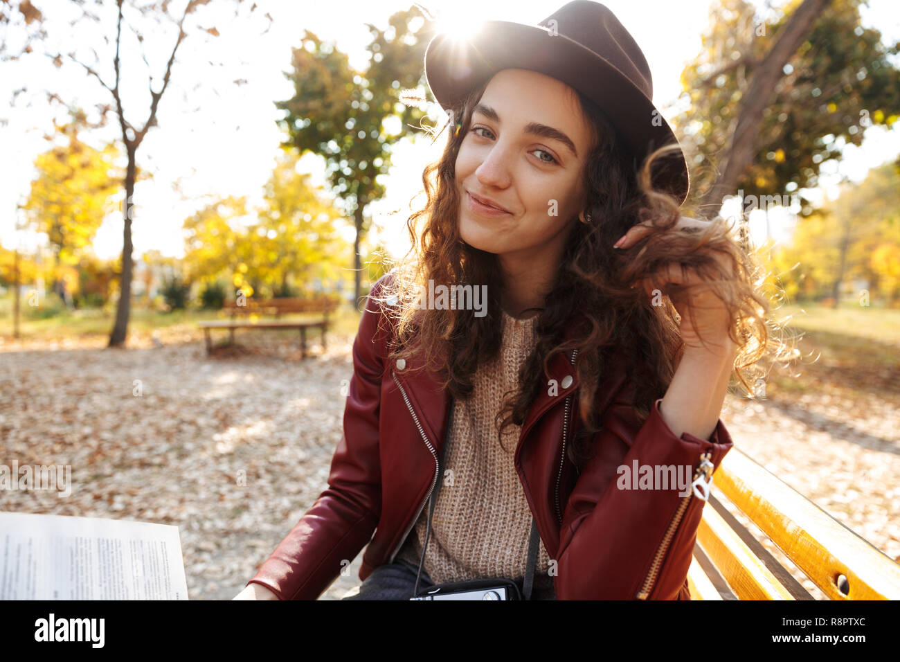 Cheerful young girl sitting on a bench at the park, reading book Stock ...