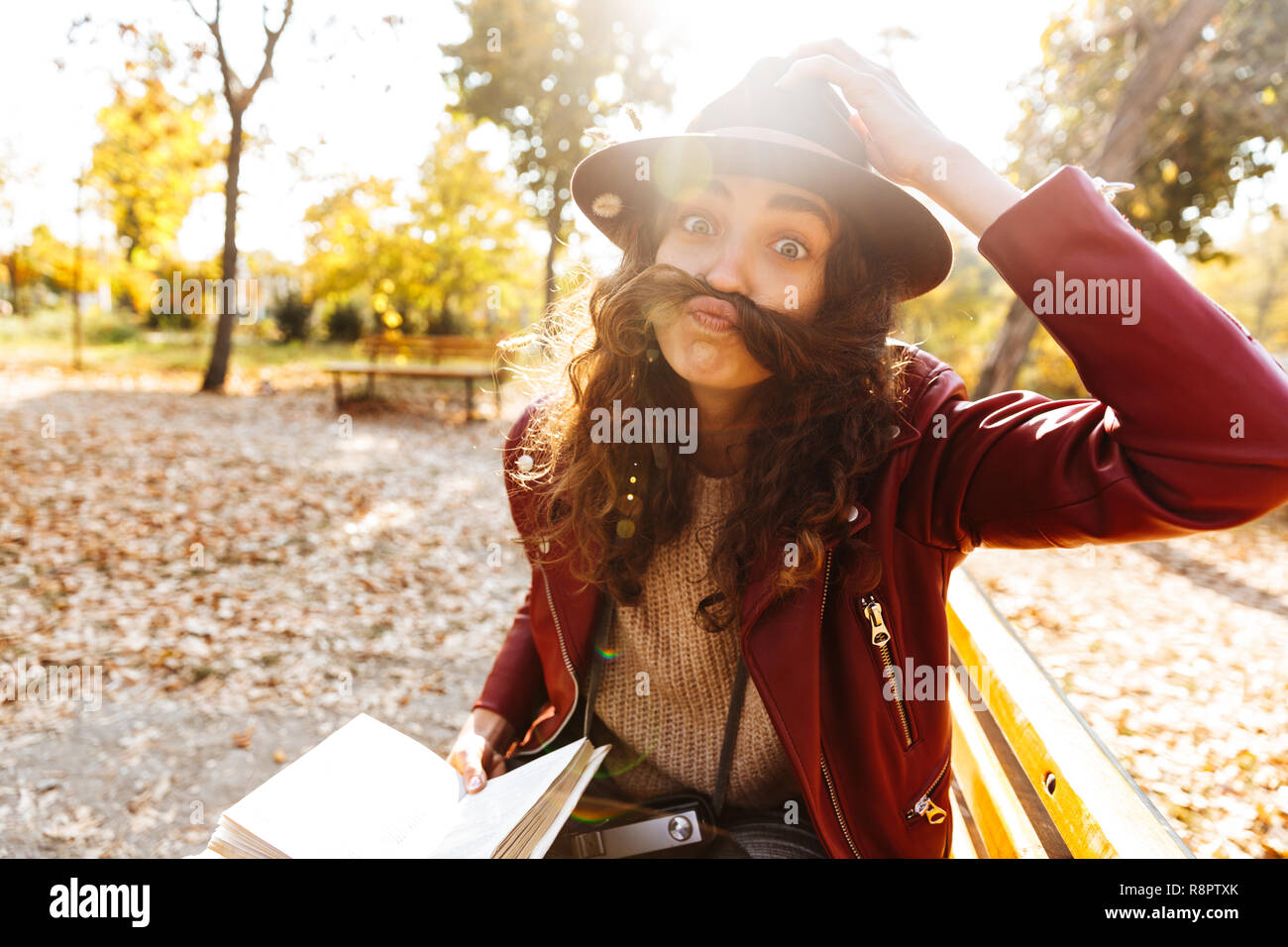 Cheerful young girl sitting on a bench at the park, reading book Stock ...