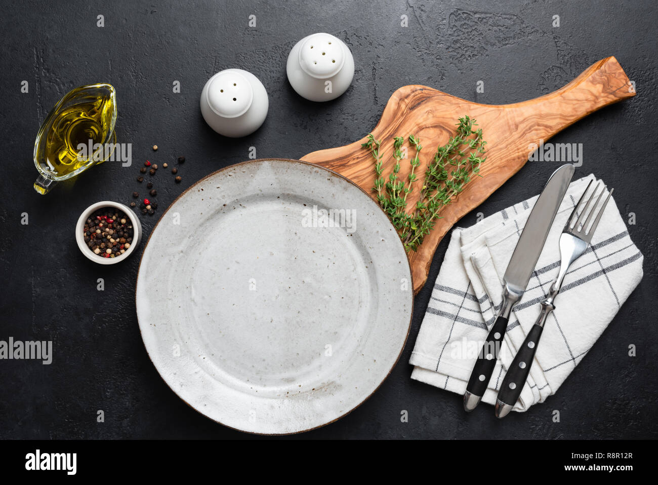 Empty plate, cutlery, olive wooden cutting board and spices on black ...