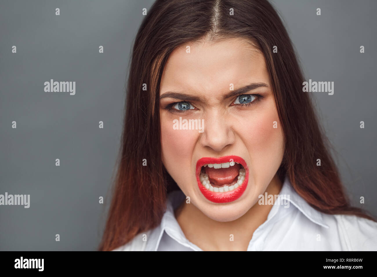 Freestyle. Woman standing isolated on grey shouting angry close-up ...