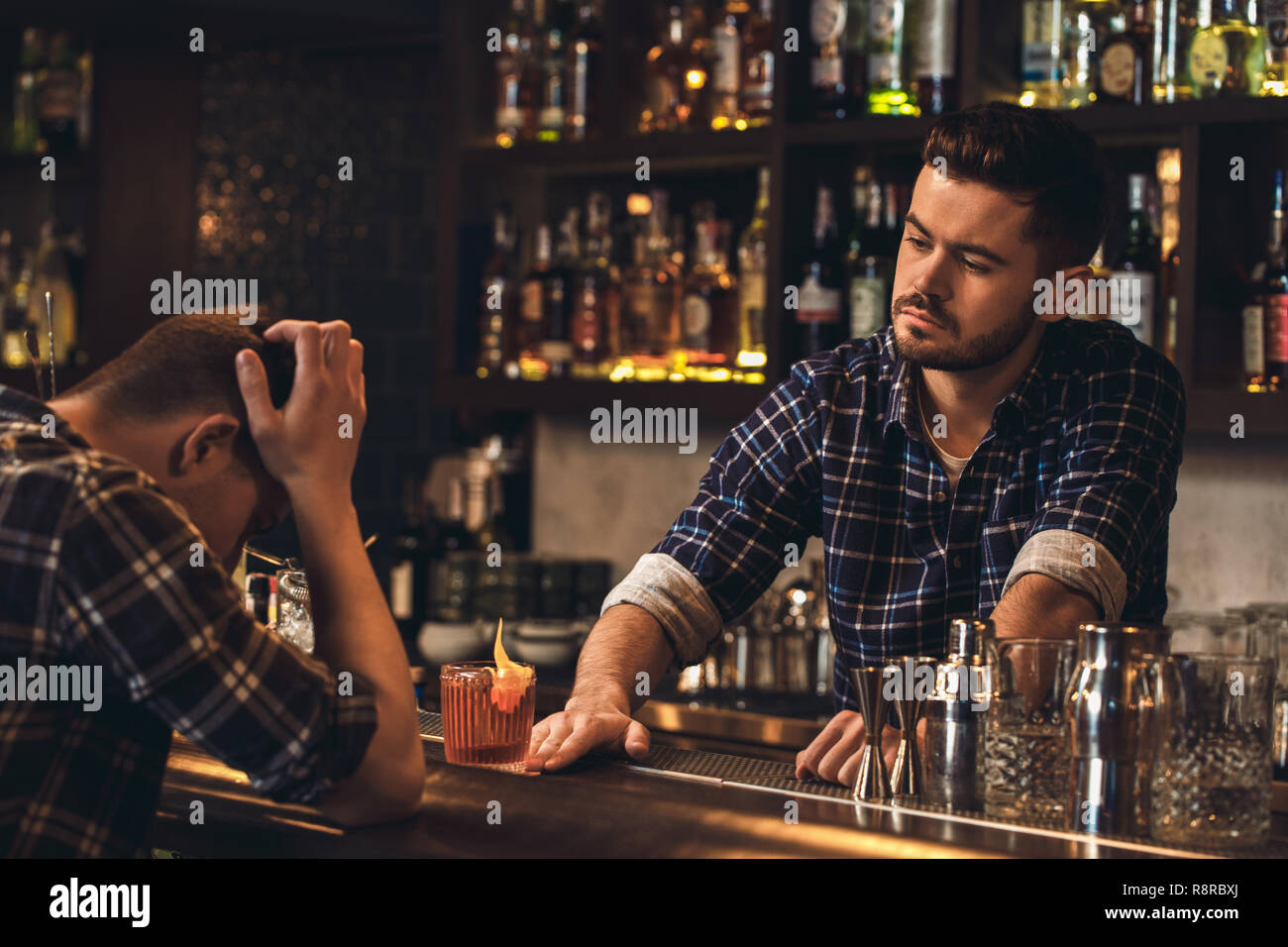 Young bartender standing at bar counter giving cocktail to sad client ...