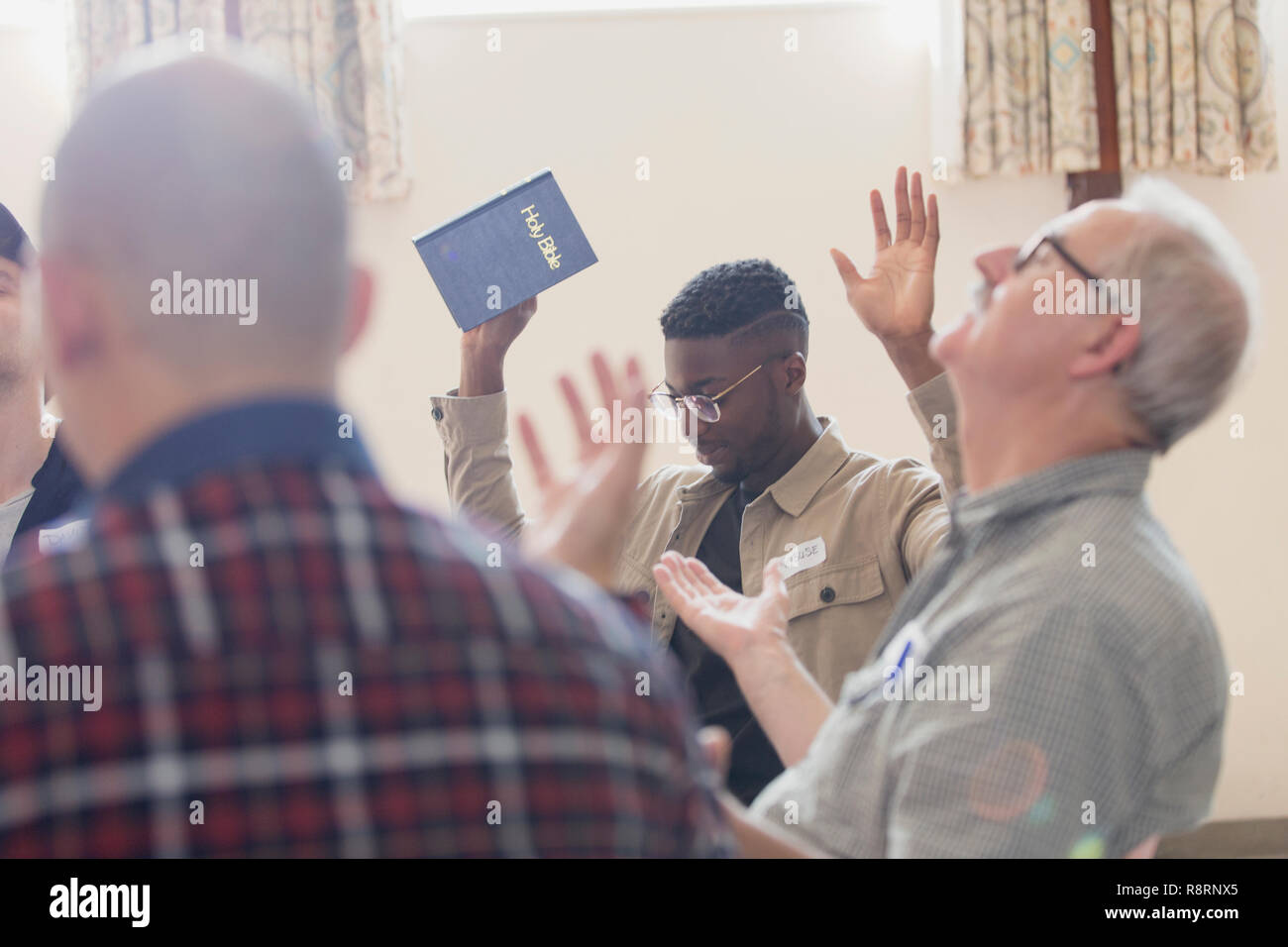 Men with bible praying with arms raised in prayer group Stock Photo - Alamy