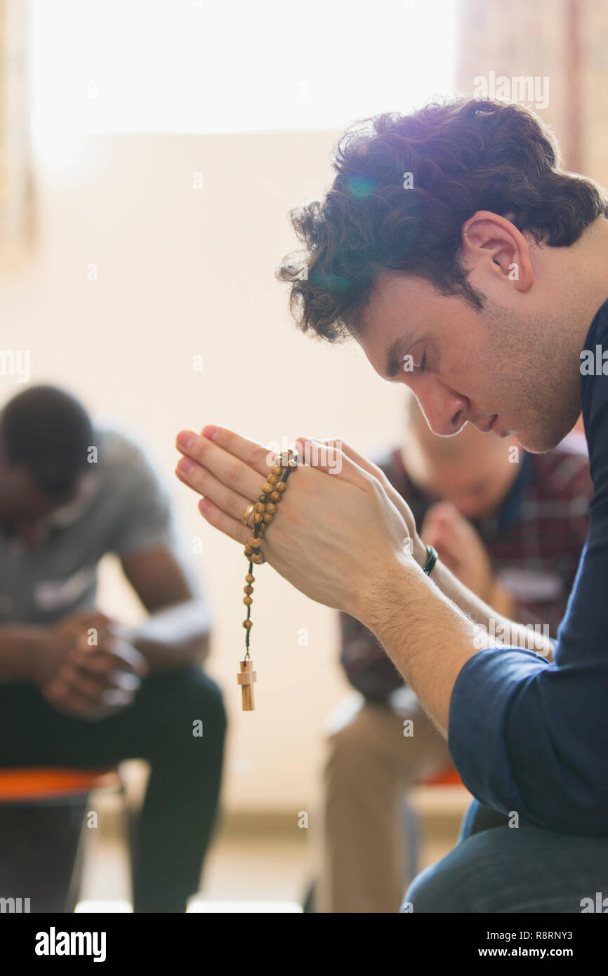 Serene man praying with rosary in prayer group Stock Photo - Alamy