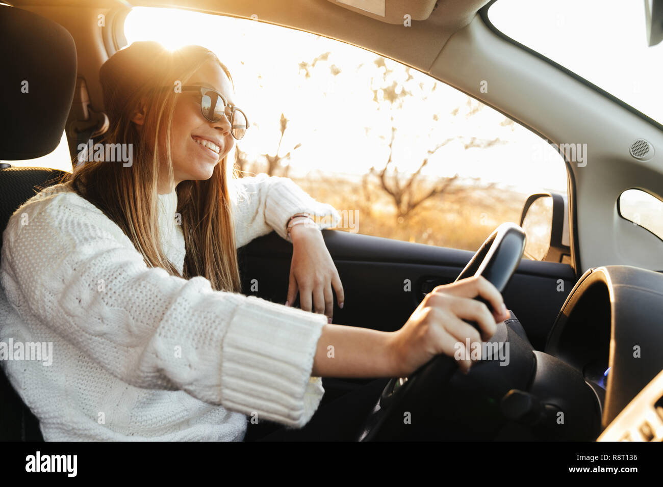 Smiling young girl driving a car during sunset Stock Photo - Alamy