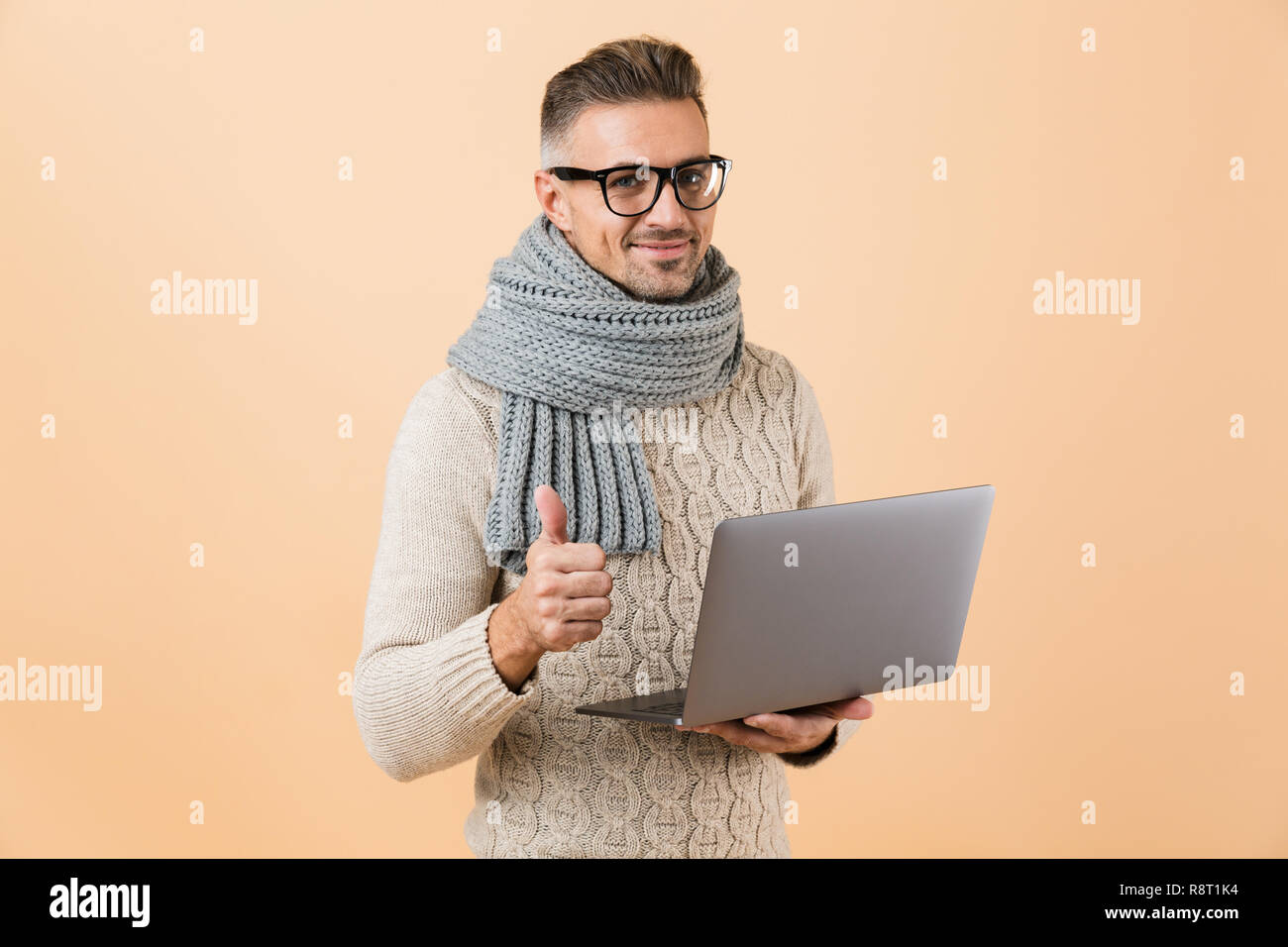 Portrait if a happy man dressed in sweater and scarf standing isolated ...