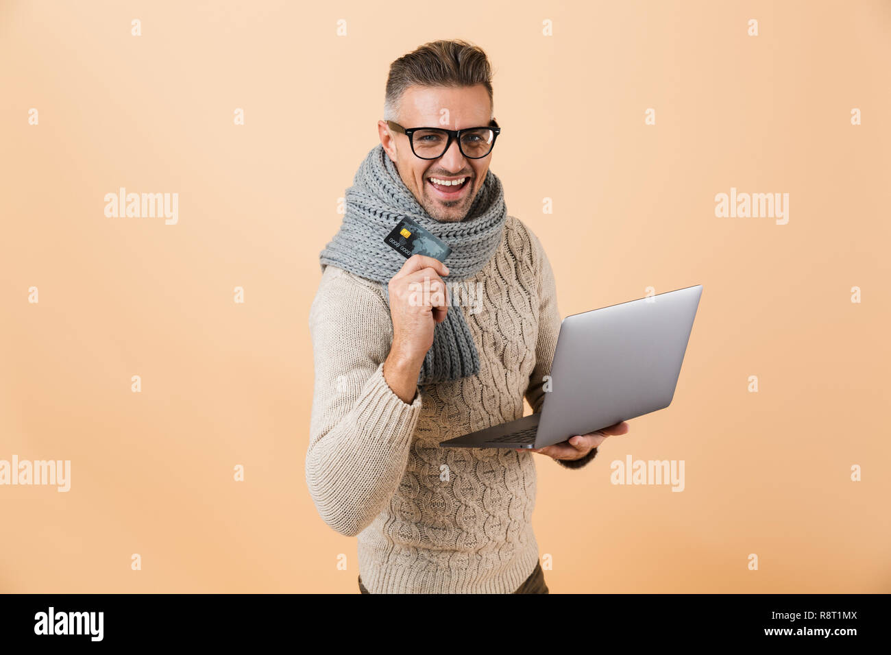 Portrait if a happy man dressed in sweater and scarf standing isolated ...