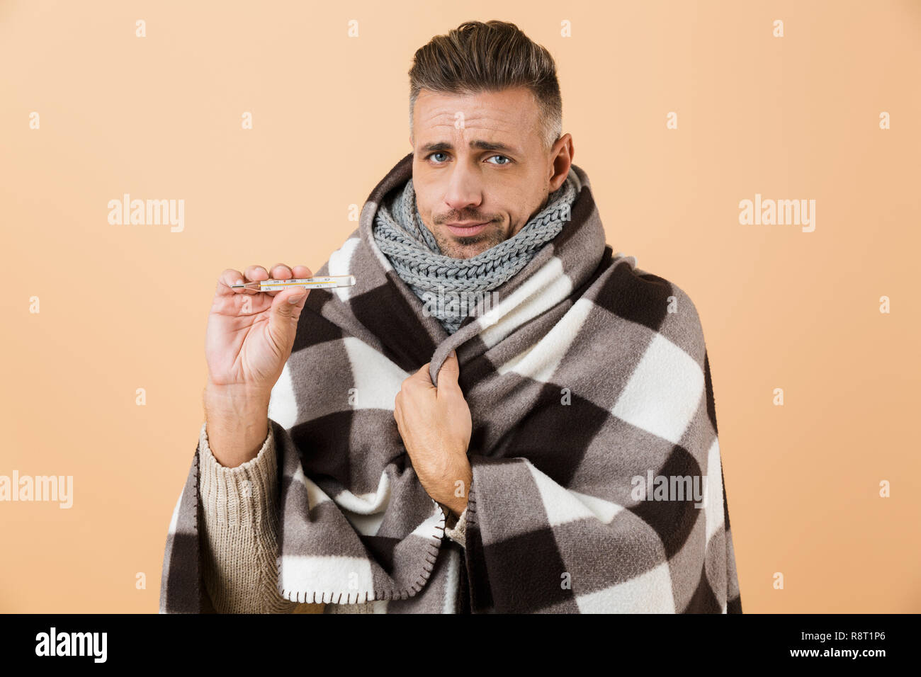 Portrait of a sick man wrapped in a blanket standing isolated over ...