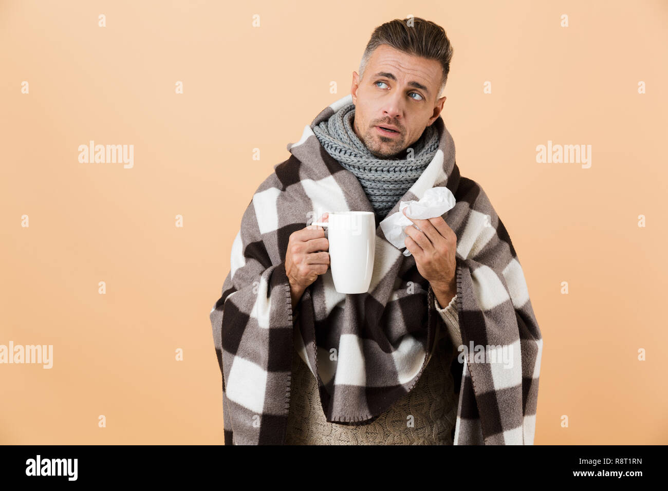 Portrait of a sad sick man wrapped in a blanket standing isolated over ...