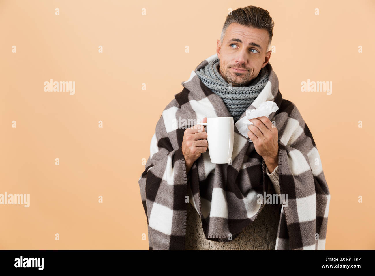 Portrait of a sick man wrapped in a blanket standing isolated over ...