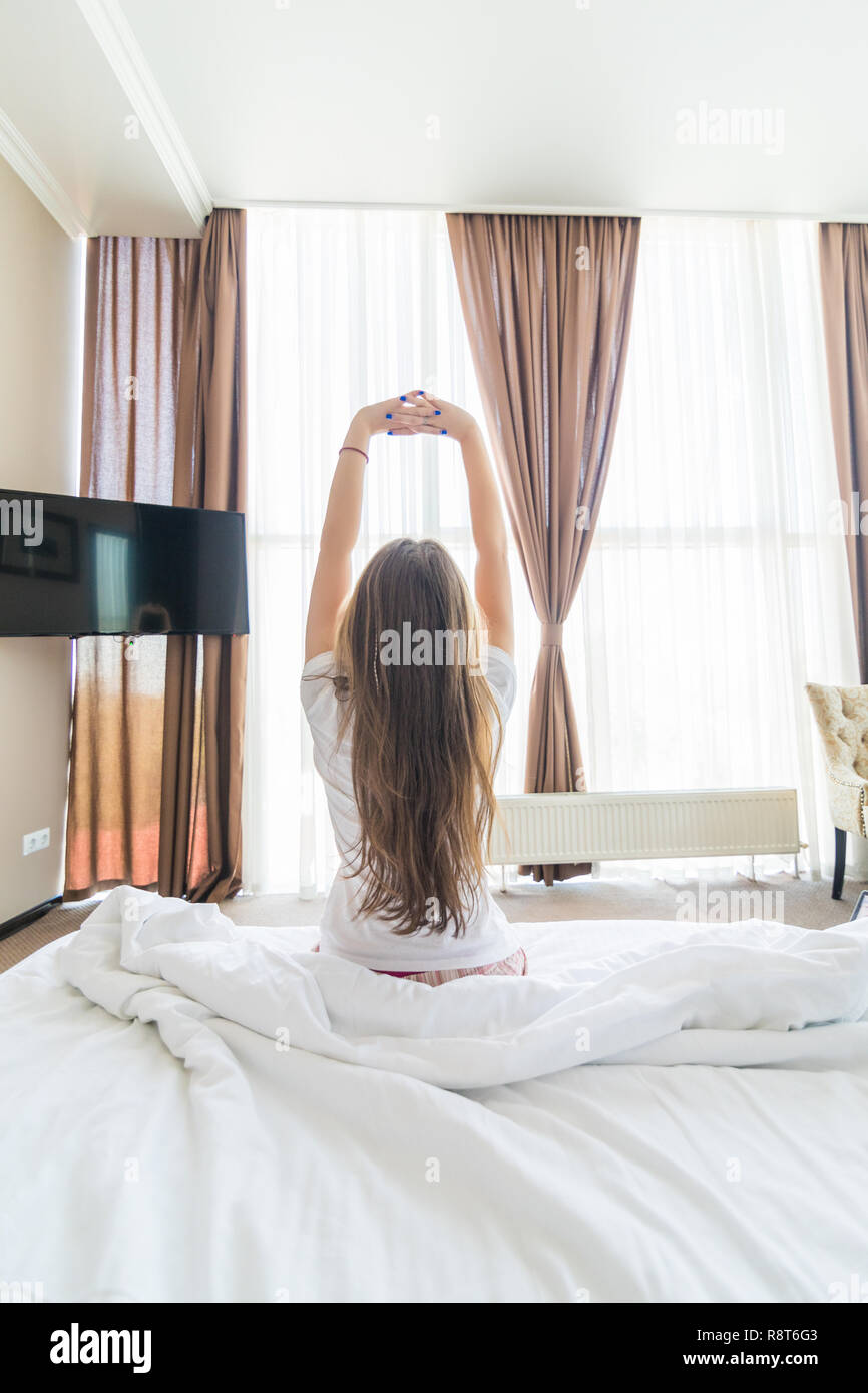 Young pretty woman outstretching her arms sitting on the bed after good ...