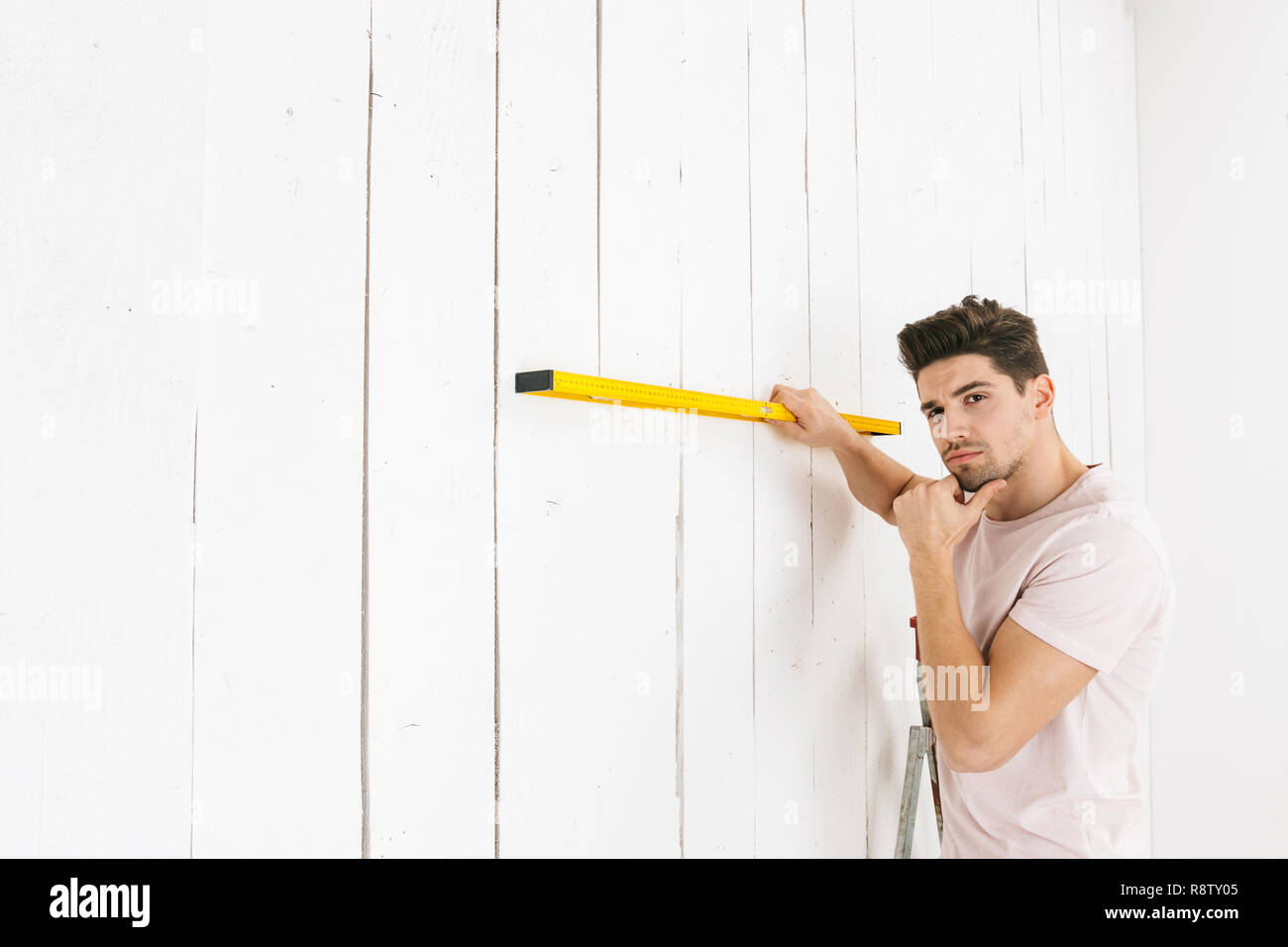 Image of handsome guy 20s holding big ruler at white wall while ...