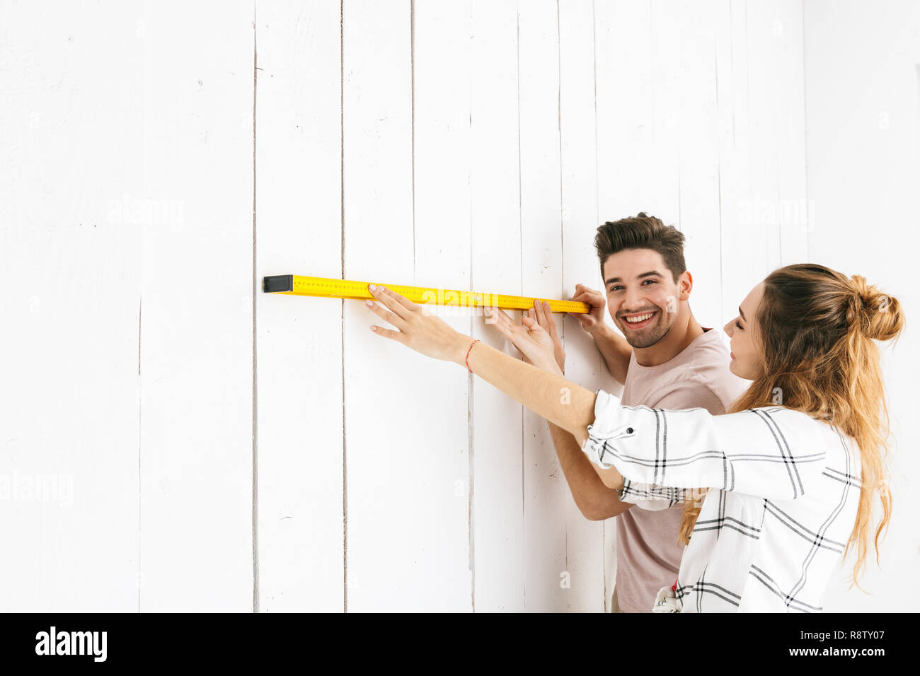 Photo of pretty couple man and woman holding big ruler at white wall ...
