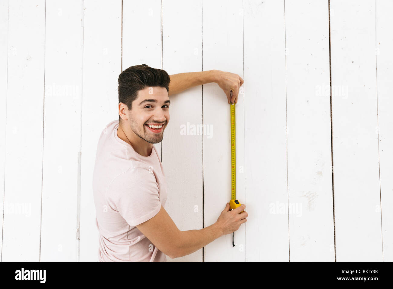 Portrait of cheerful man 20s holding yellow ruler for measurement over ...