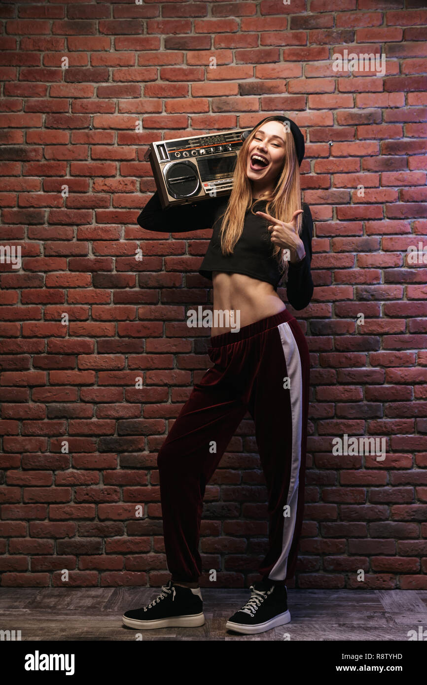 Full length image of modern hip hop woman 20s standing against brick ...