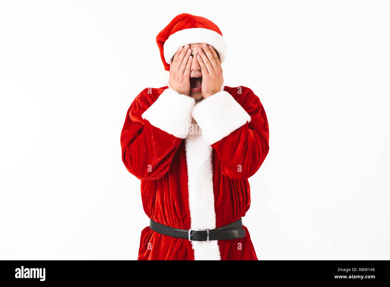 Portrait of scared man 30s in santa claus costume and red hat grabbing ...