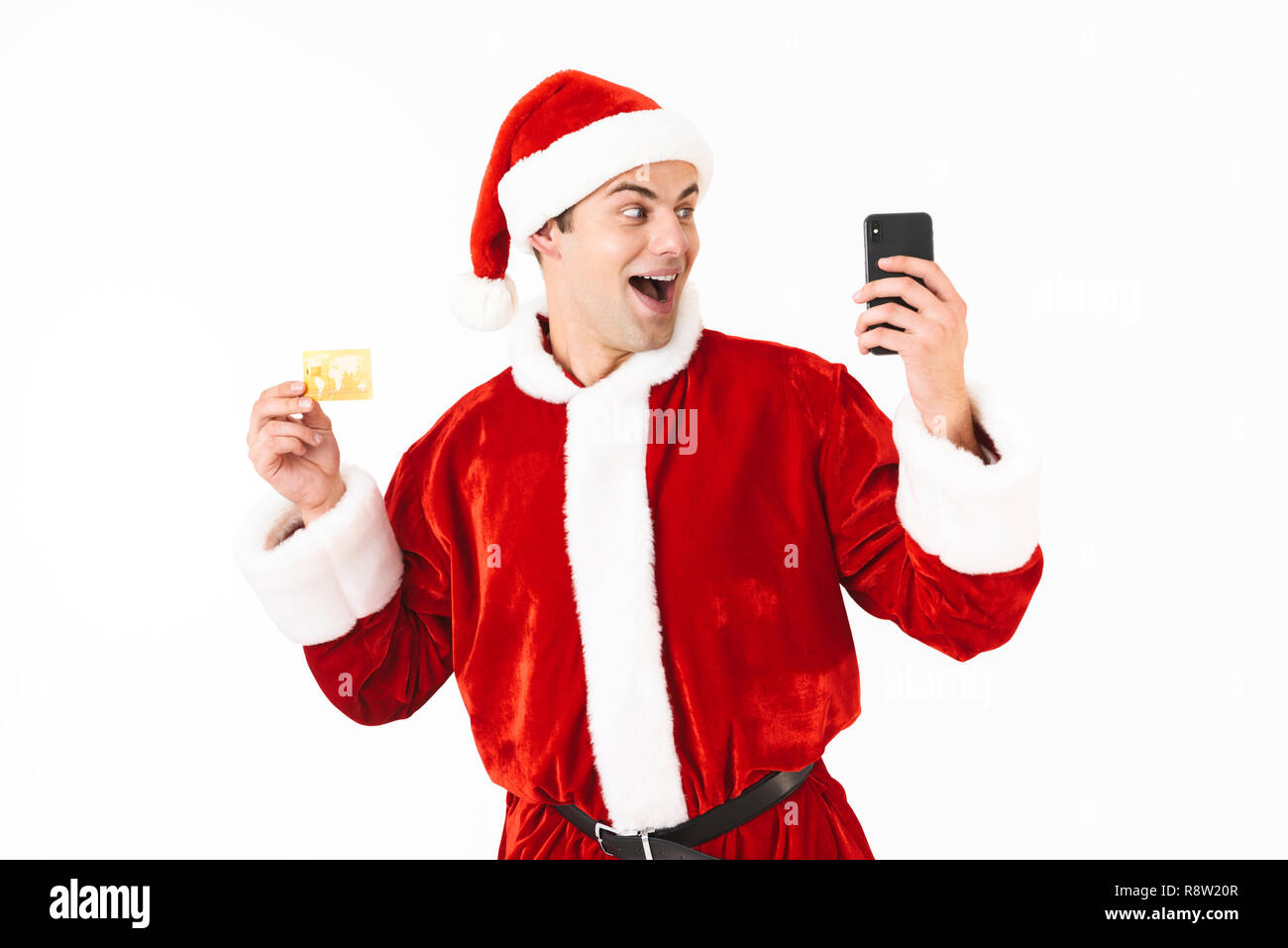 Photo of cheerful man 30s in santa claus costume holding smartphone and ...