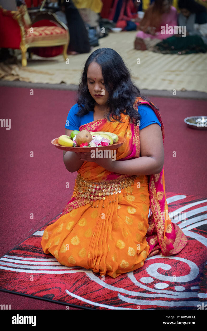 A devout Hindu woman in a beautiful orange sari kneels in prayer & in ...