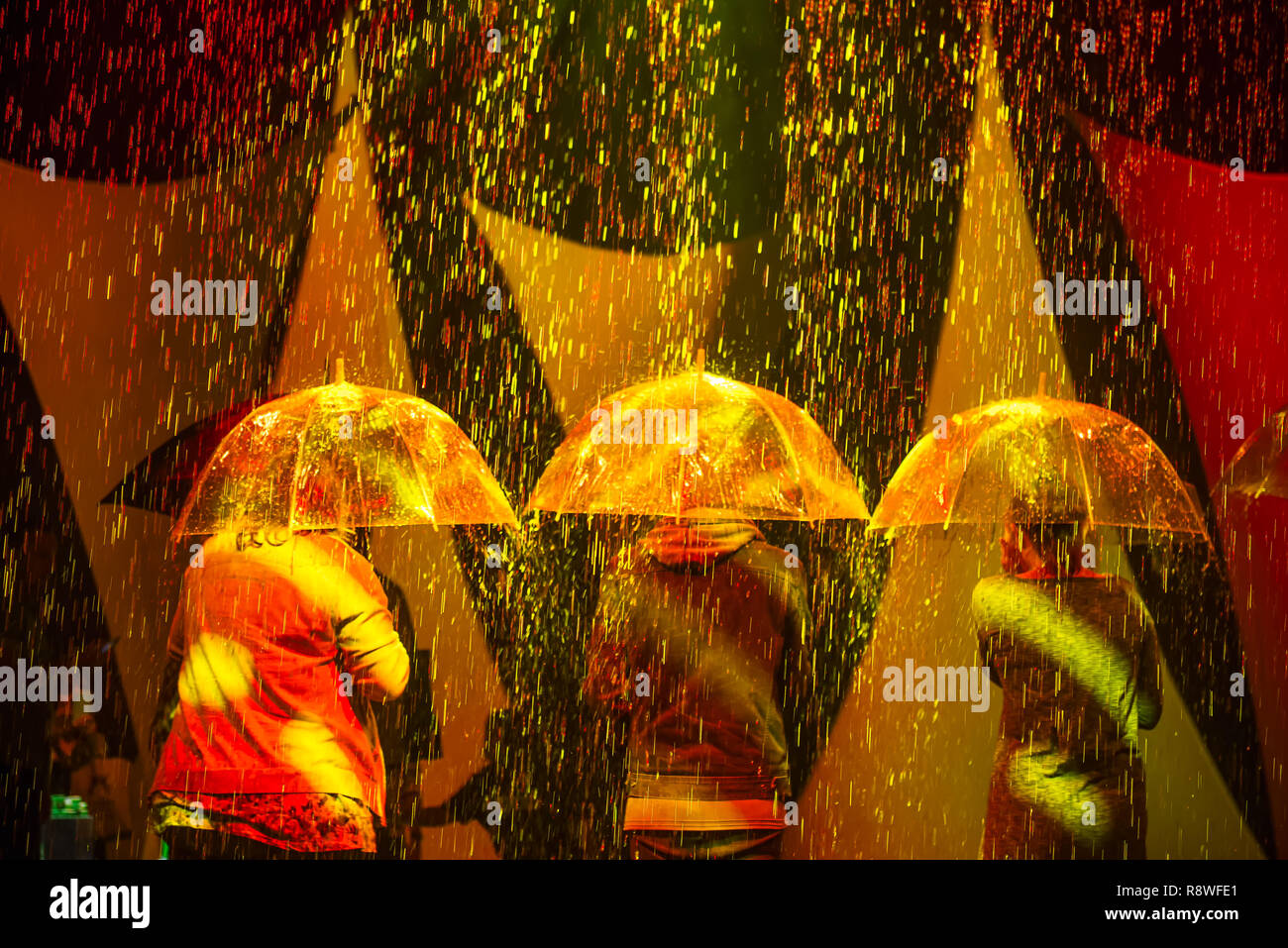 Back view three persons with umbrellas under artificial rain coming ...