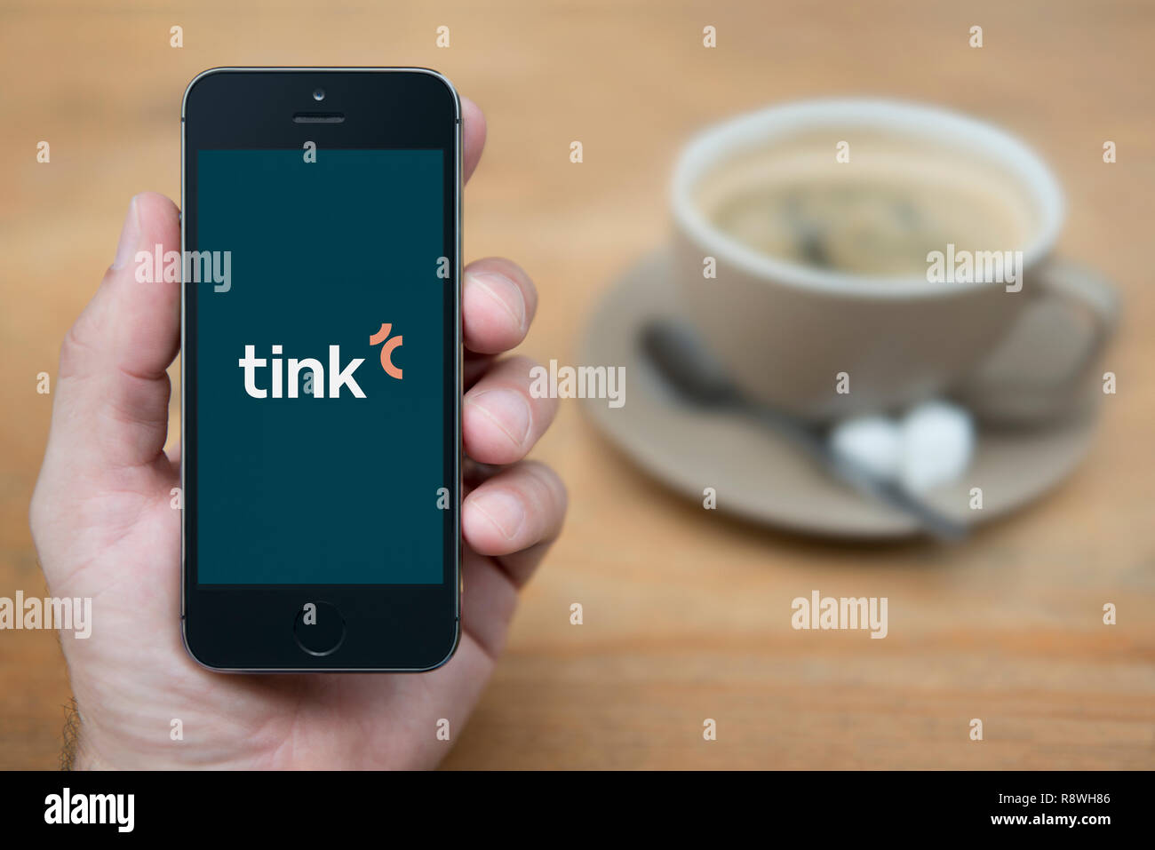 A man looks at his iPhone which displays the Tink logo (Editorial use ...
