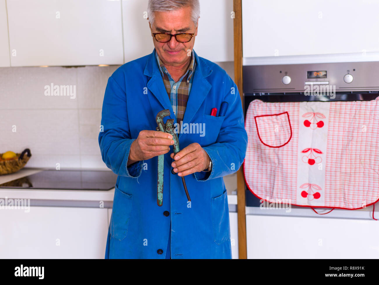 Old age handyman standing in the kitchen and working with pilers Stock ...