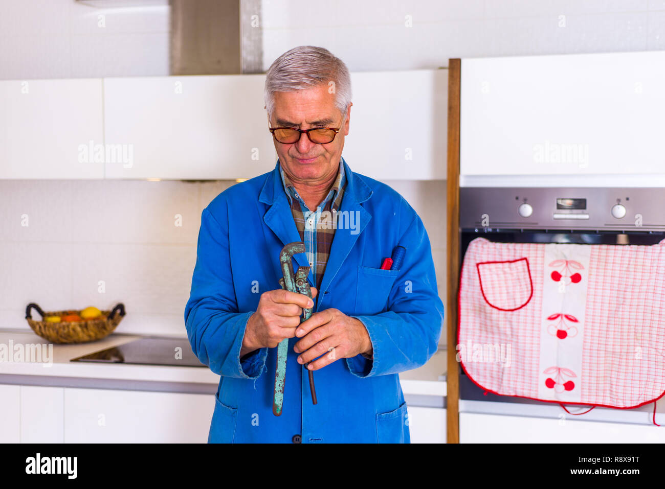 Old age handyman standing in the kitchen and working with pilers Stock ...