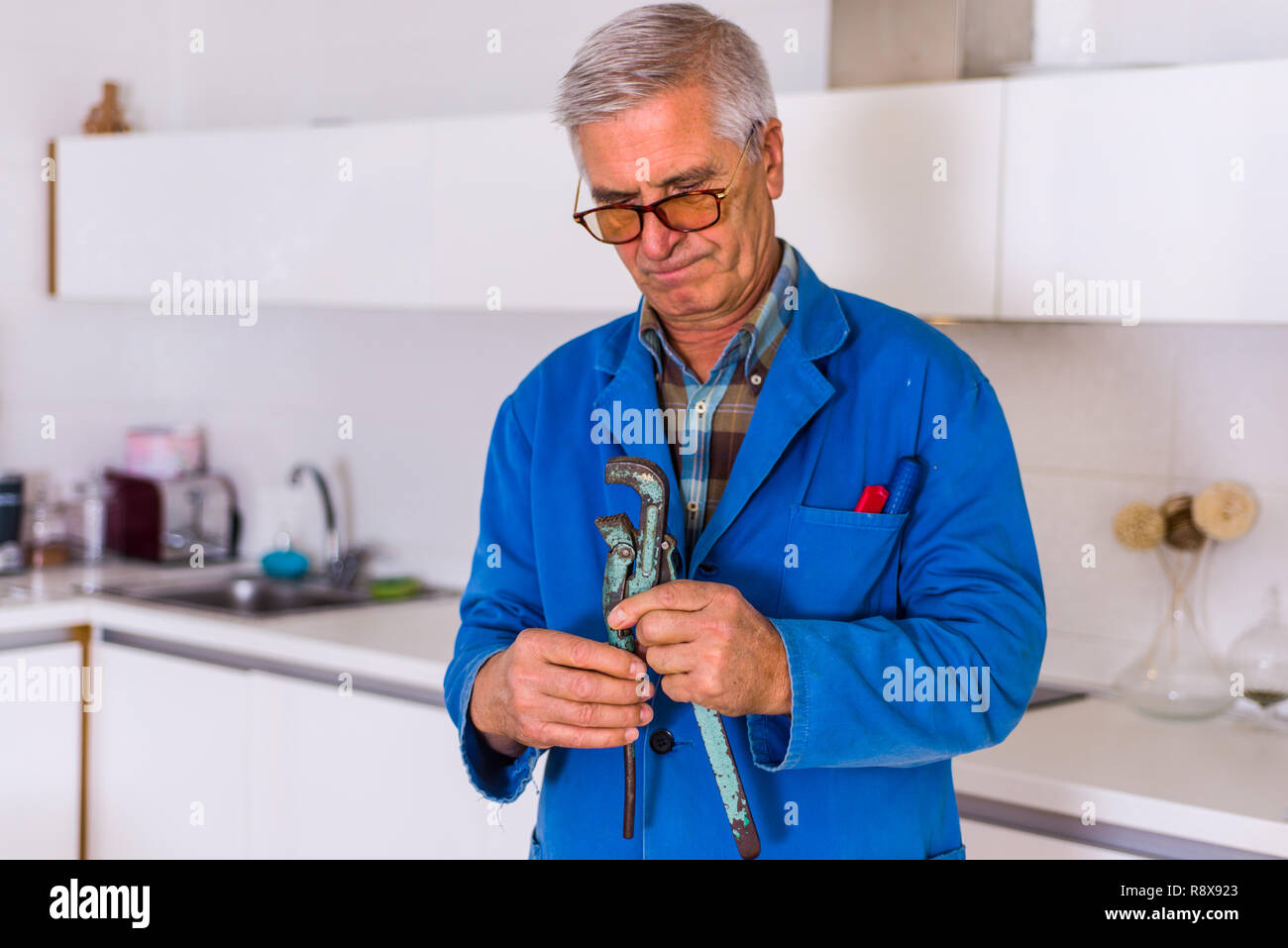 Serious male repairman holding pilers and working inside the kitchen ...