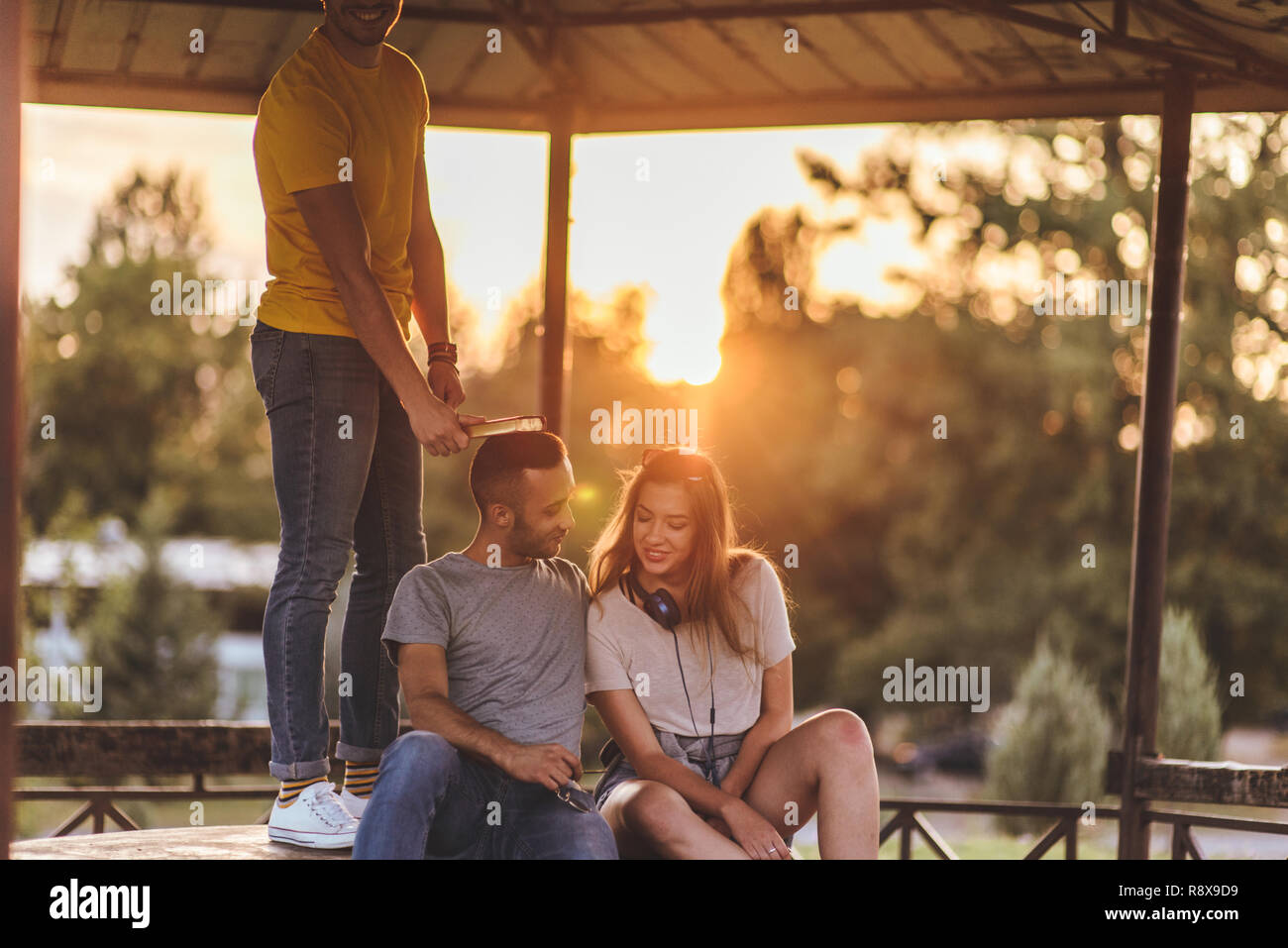 Three friends are enjoying beautiful sunset in the park, smiling and ...
