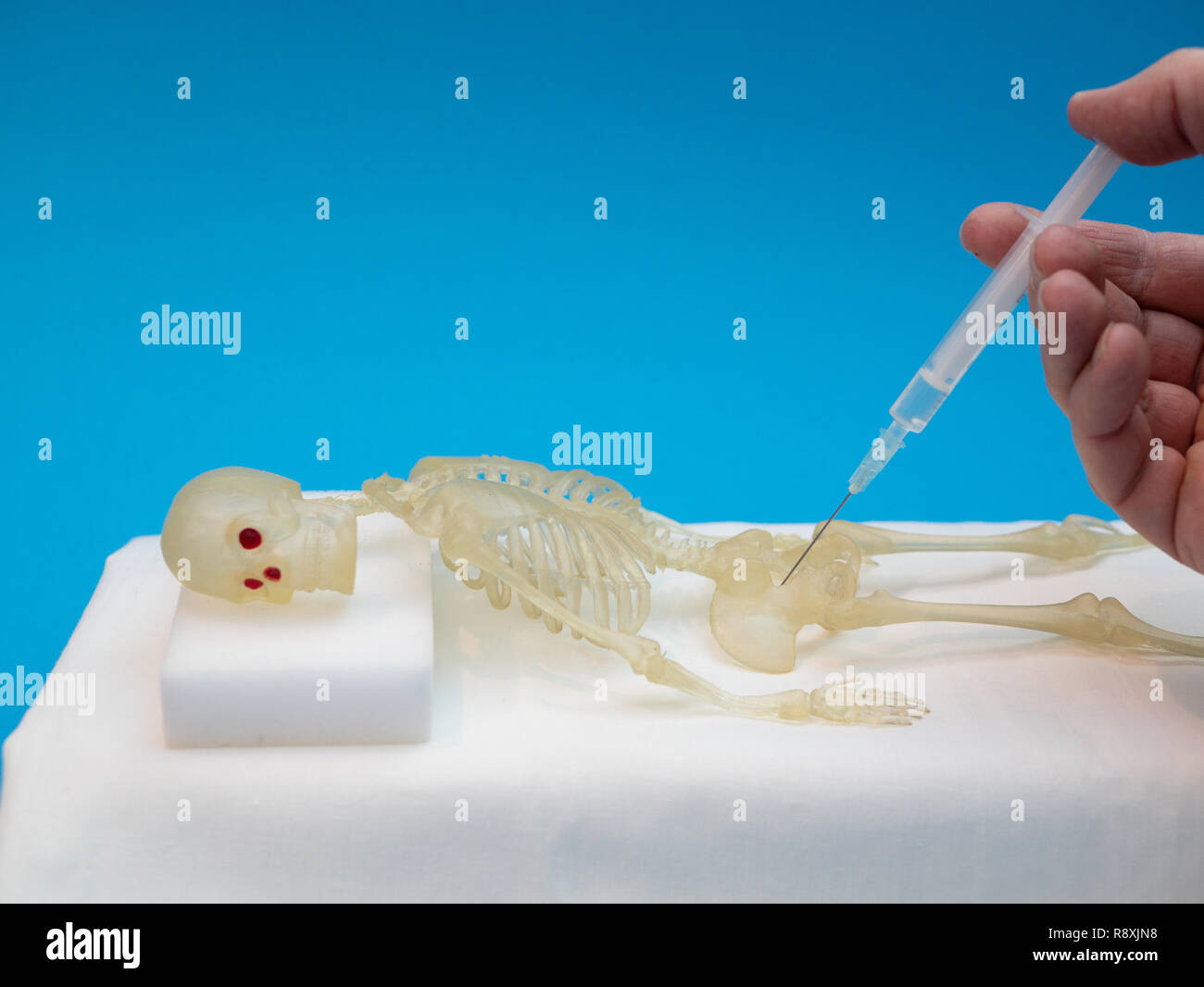 hand with syringe doing injection in butt of human skeleton lay on ...