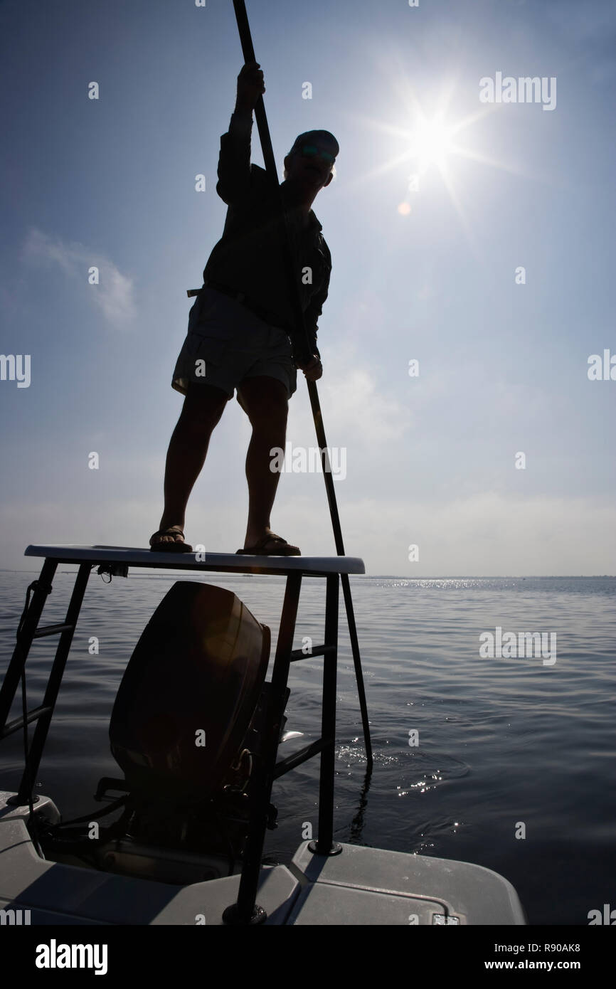 A fly-fishing guide poling a flats boat poling skiff off the shoreline ...