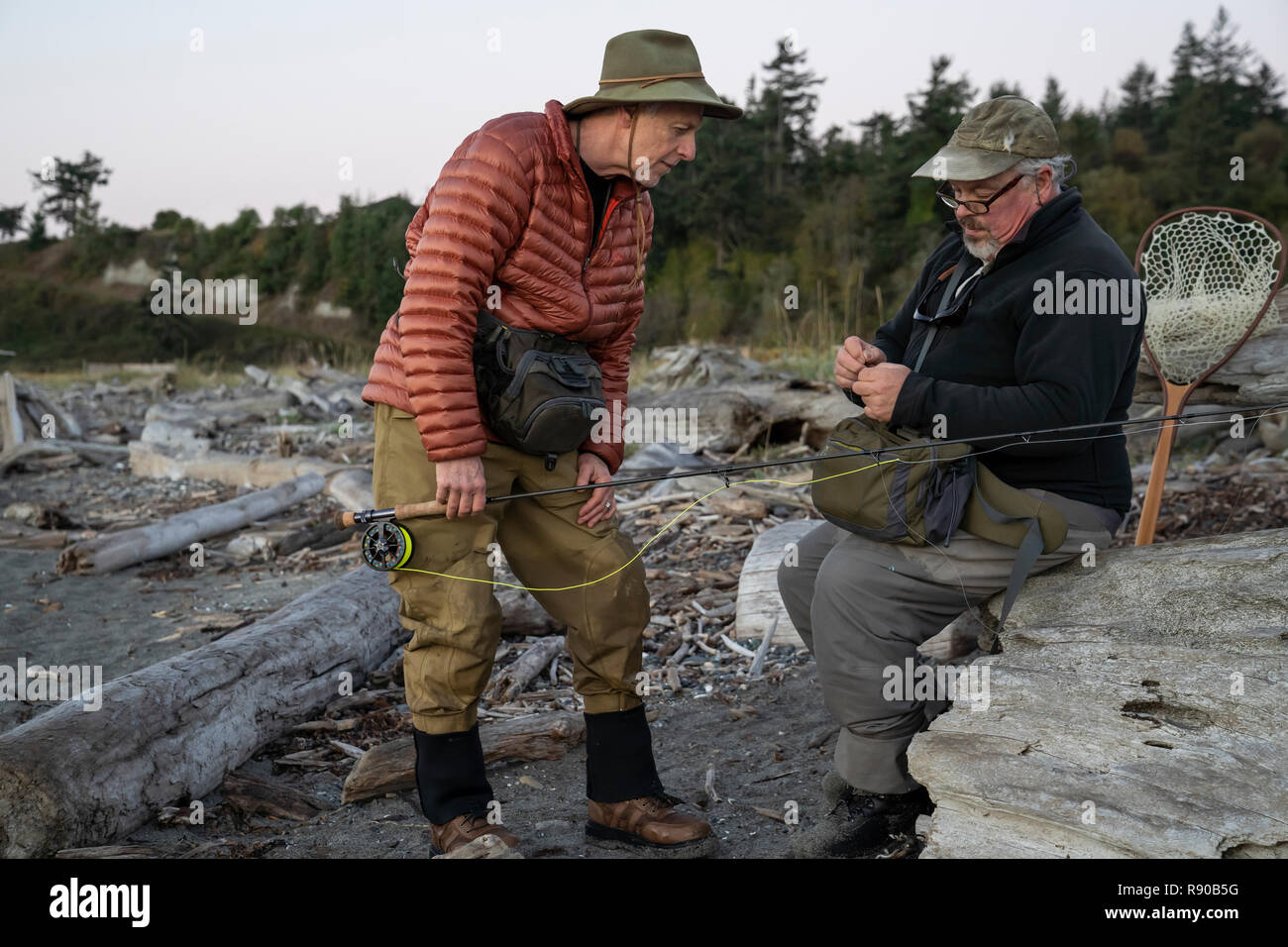 A male fly fisherman watches his guide work putting on a new fly to try ...