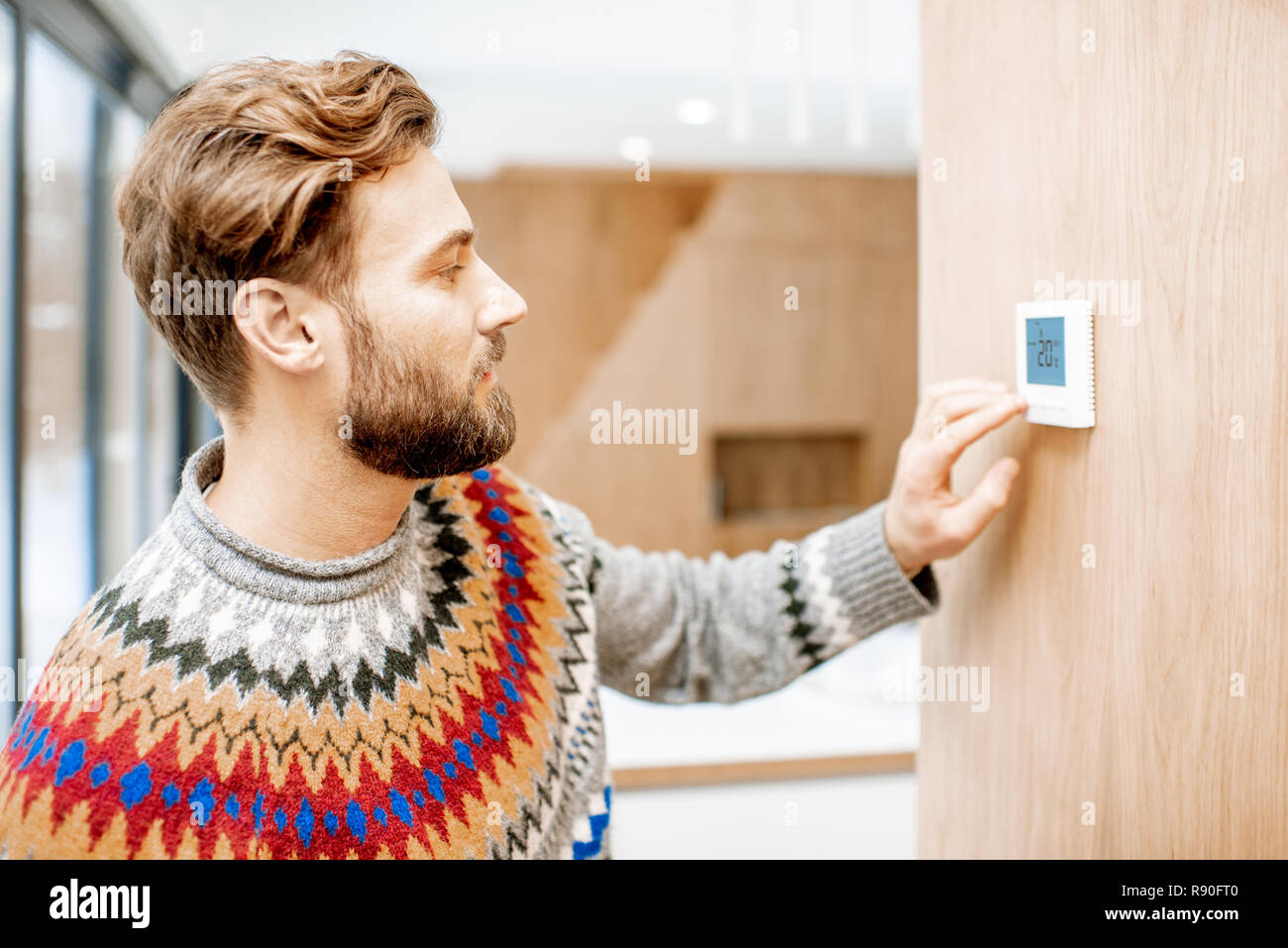 Man in sweater feeling cold adjusting room temperature with electronic ...