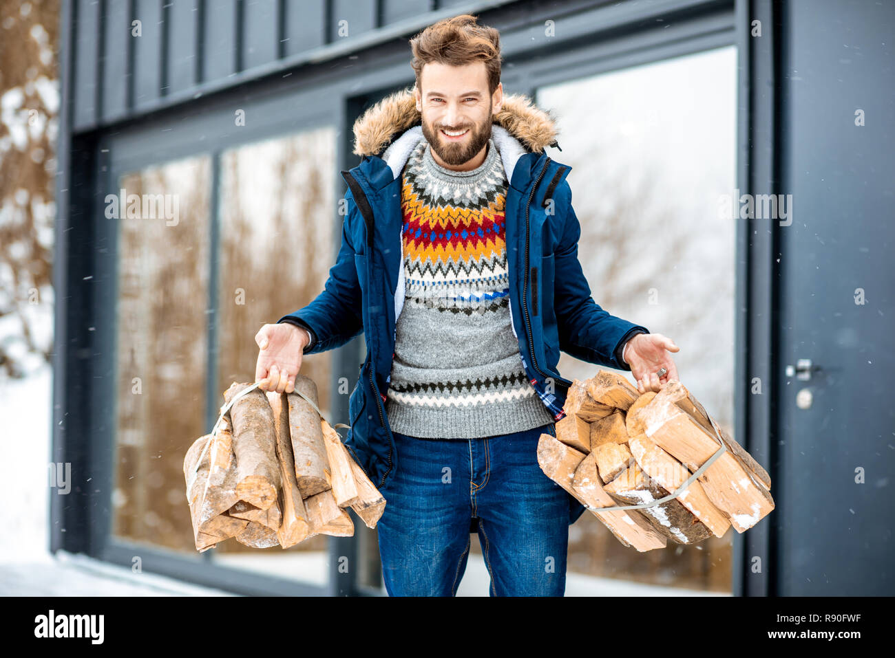 Handsome man in winter clothes carrying firewoods on the terrace near ...