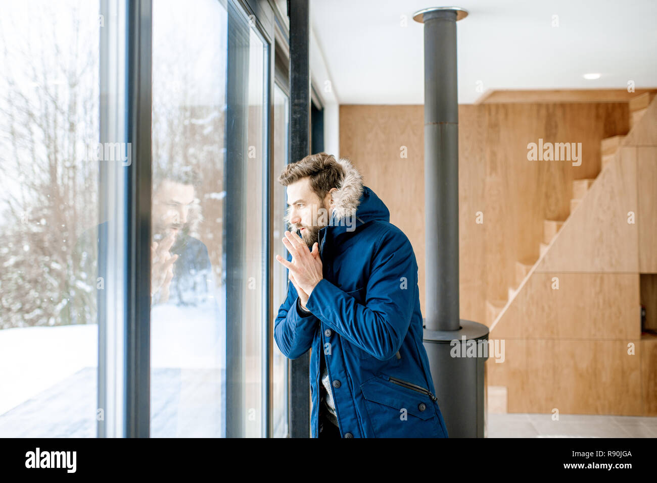 Man dressed in winter clothes feeling cold standing near the window at ...