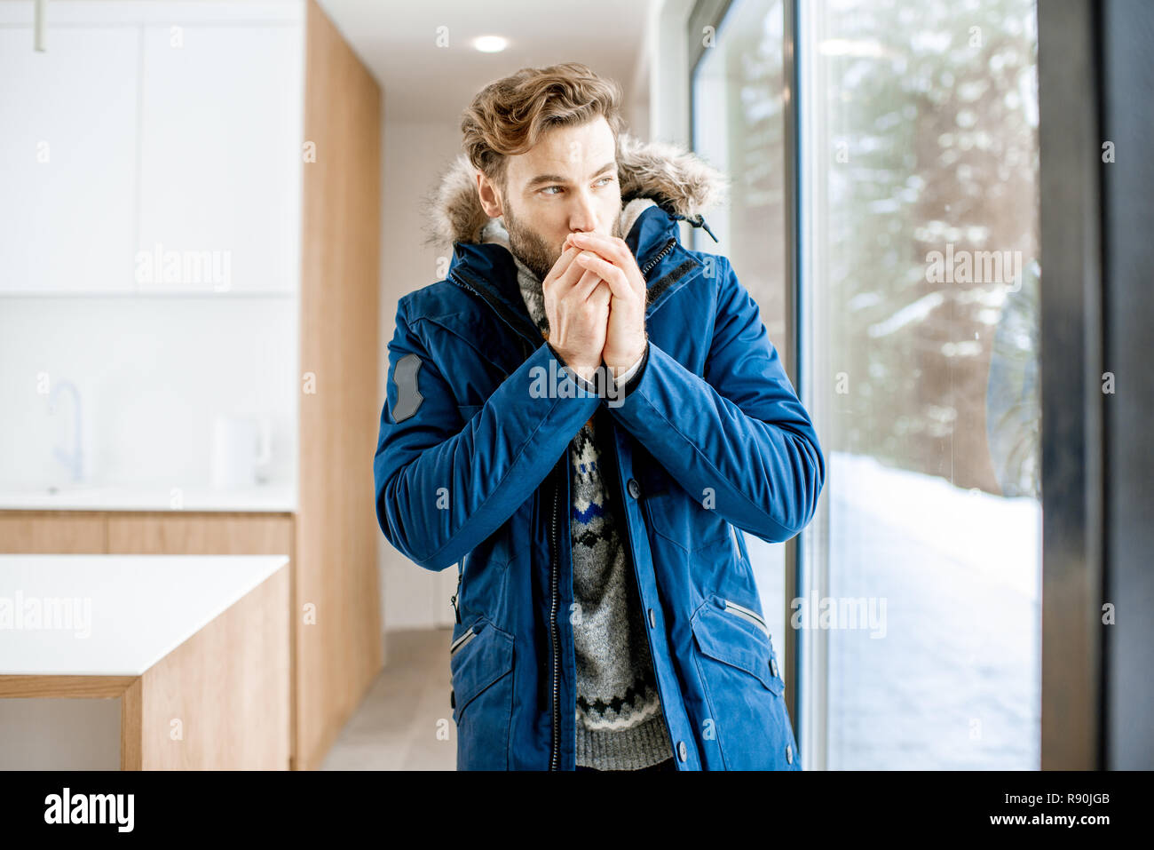 Man dressed in winter clothes feeling cold standing near the window at ...