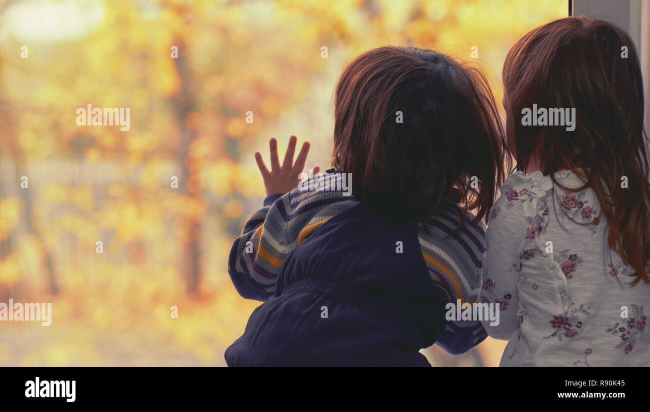 Kids by the window looking outside. Outside the window is autumn and ...