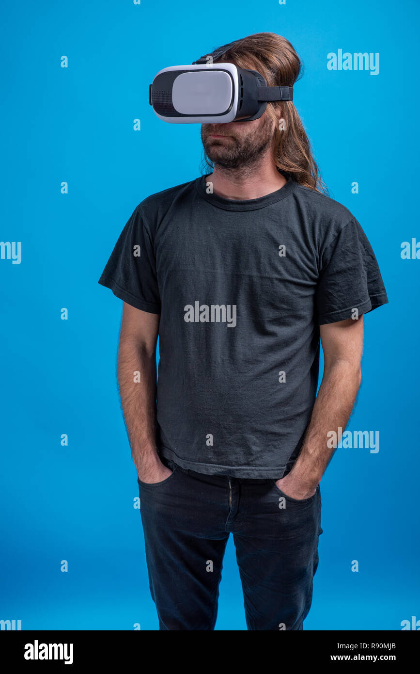 Male wearing VR device with hands in pockets standing still looking ...