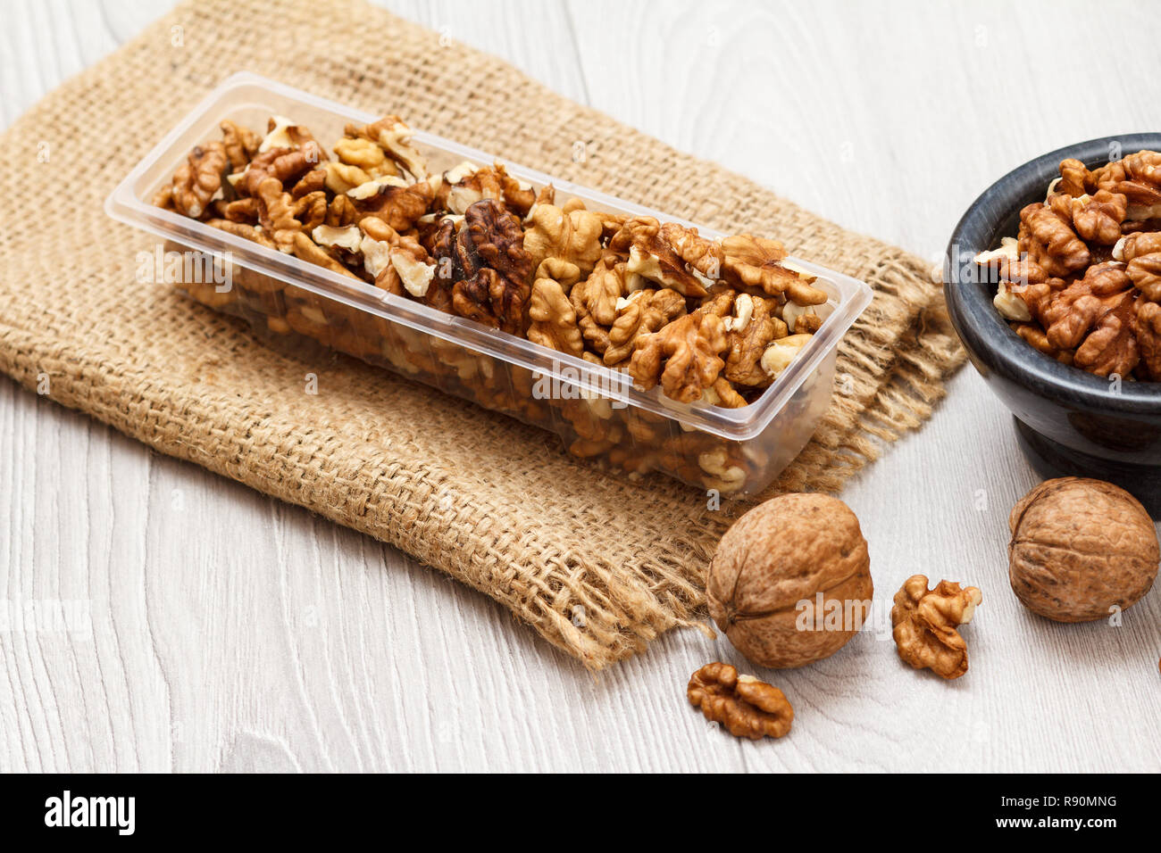Peeled walnuts in plastic container and stone bowl with sackcloth on a ...