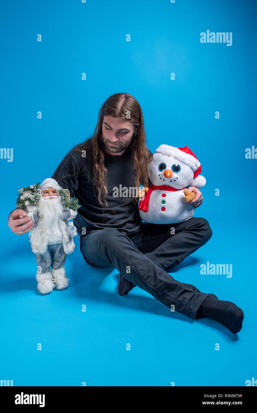 Long-haired man looking down at Santa's toy while holding a snowman and ...