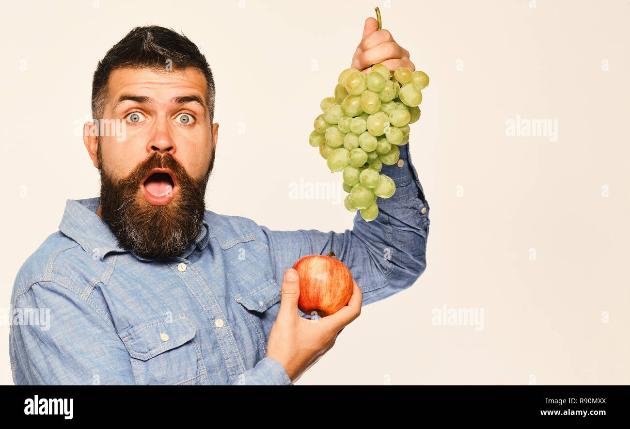 Farmer shows harvest. Winegrower with shocked face holds grapes and red ...