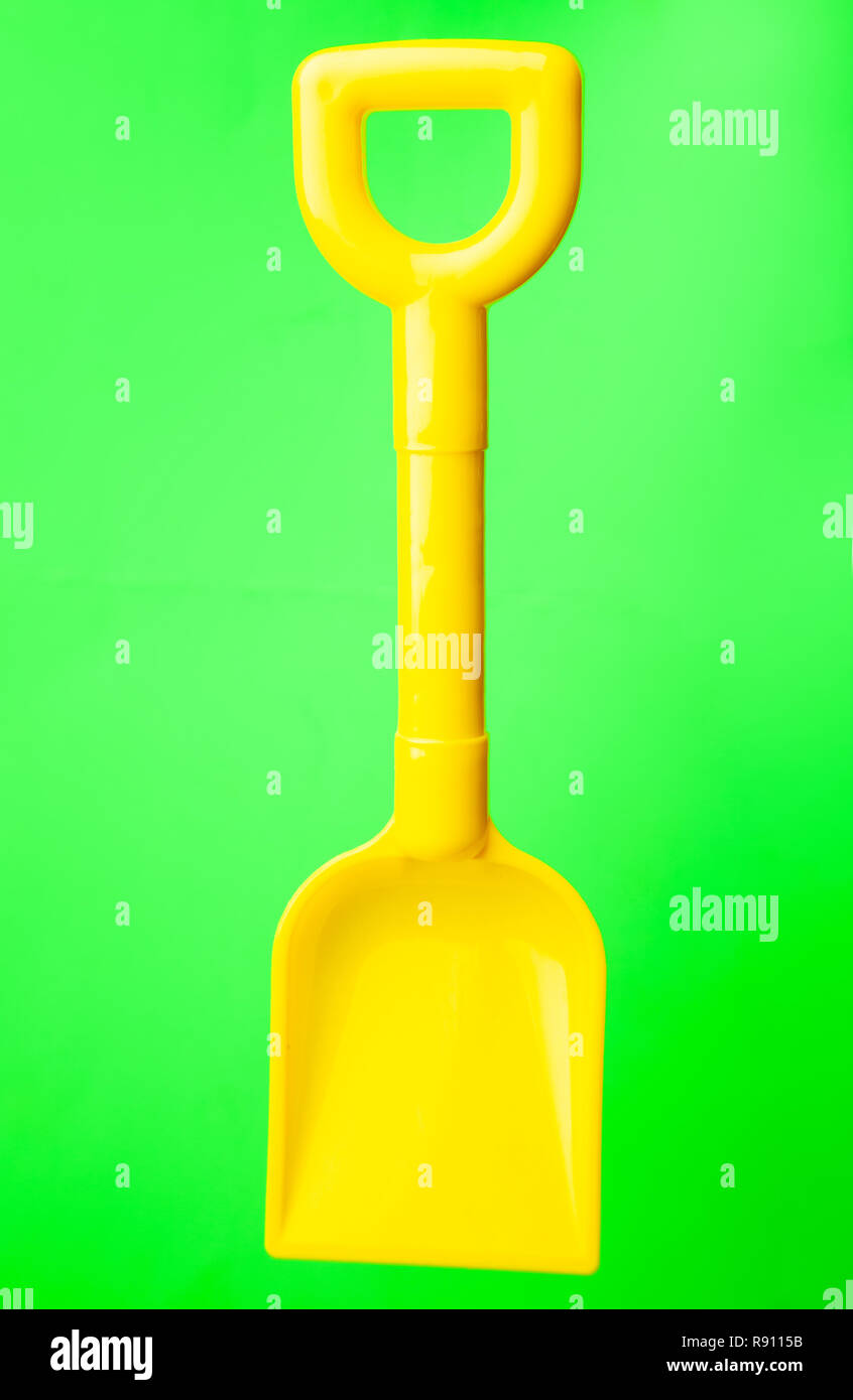 A plastic yellow toy spade against a green background Stock Photo - Alamy