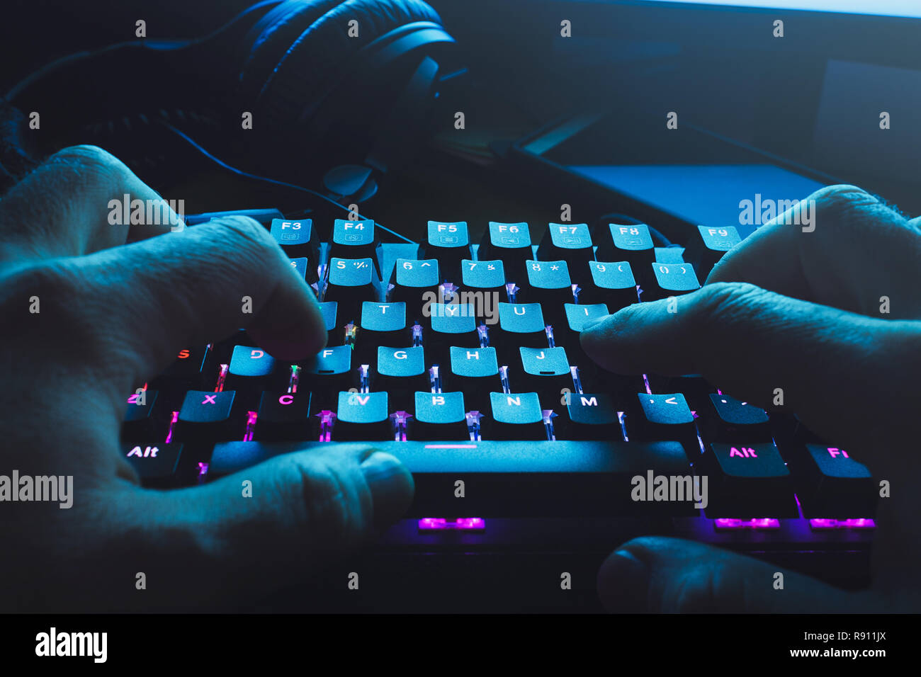 Male hands typing on the black illuminated keyboard with blue light ...