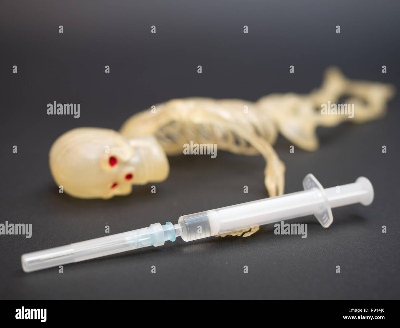 toy skeleton lay on the ground with syringe in hand on dark black ...