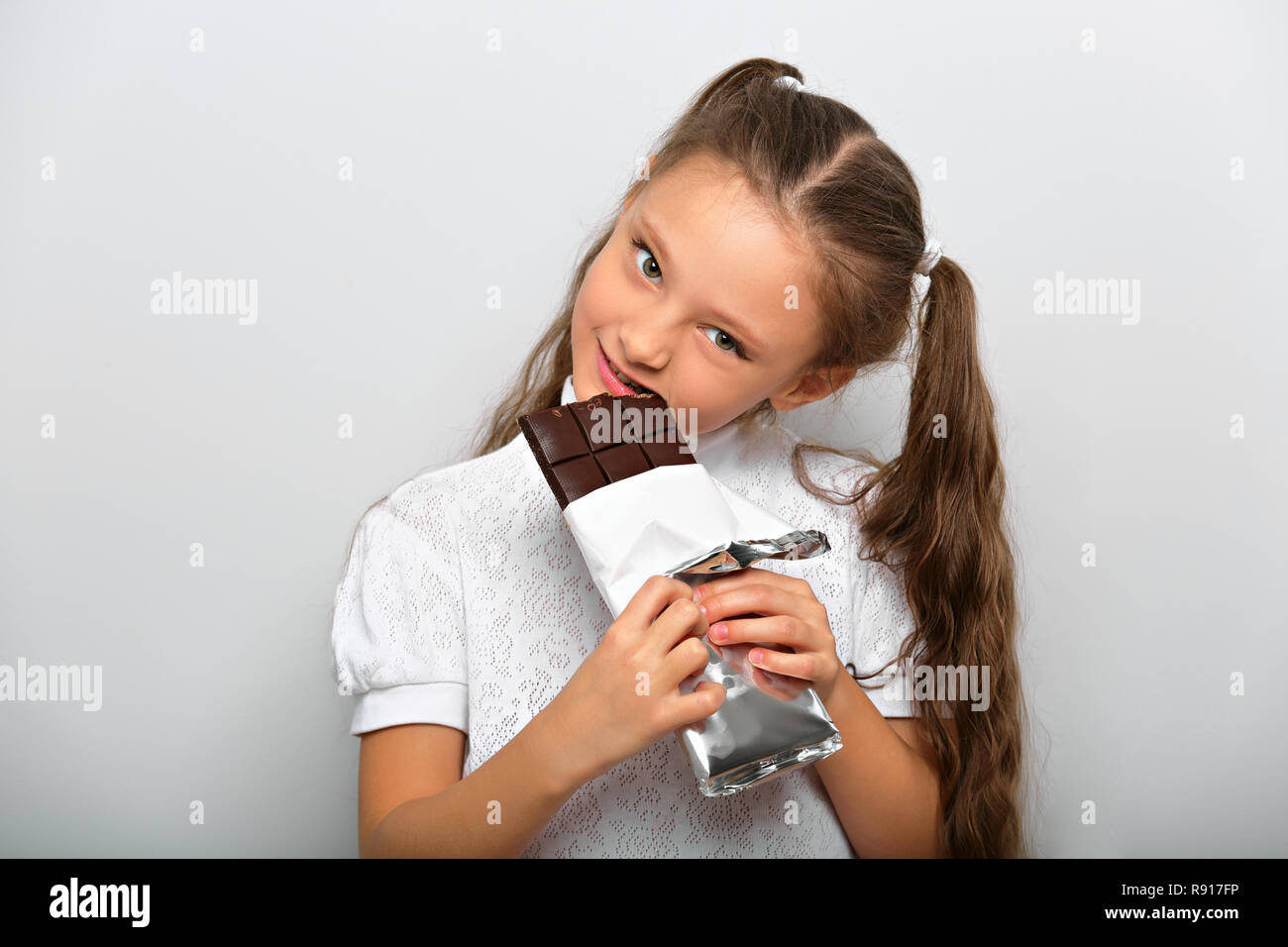 Happy fun smiling kid girl biting dark chocolate with craving eyes ...