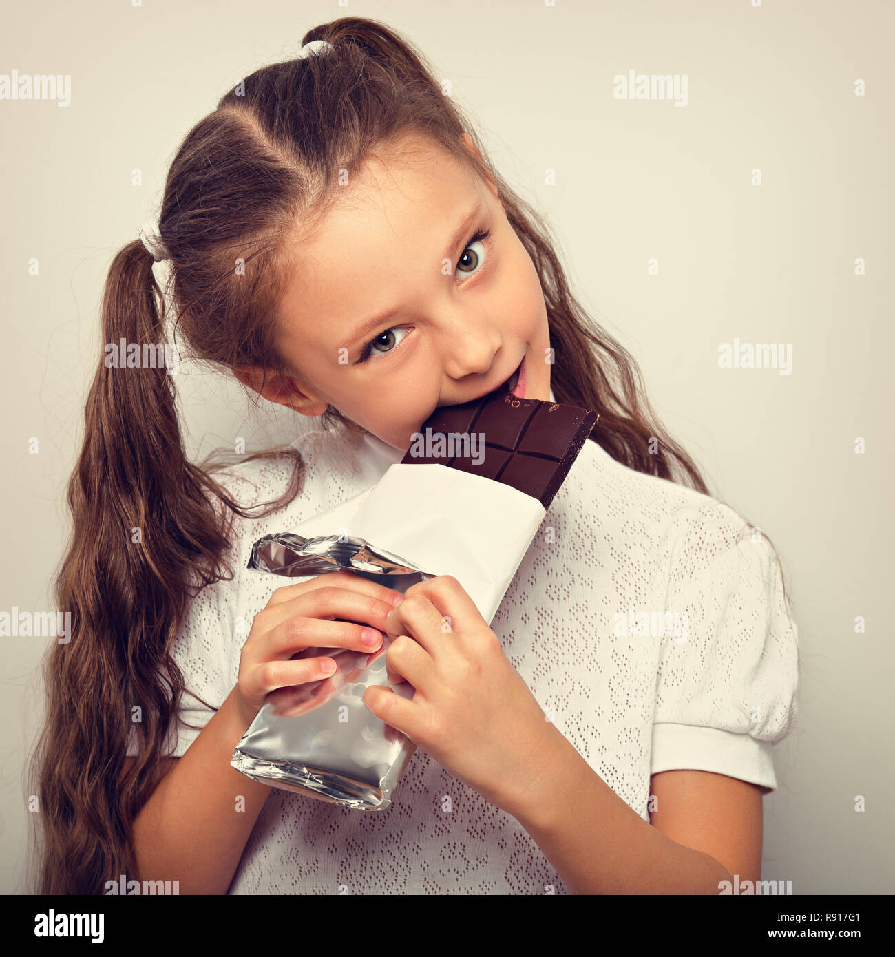 Happy fun smiling kid girl biting dark chocolate with craving eyes ...