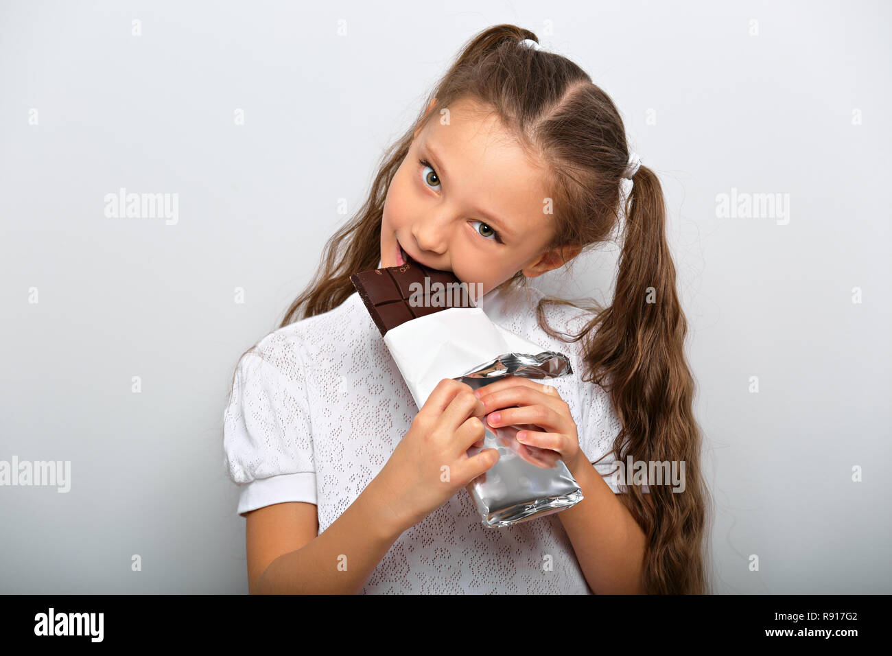 Happy fun smiling kid girl biting dark chocolate with craving eyes ...