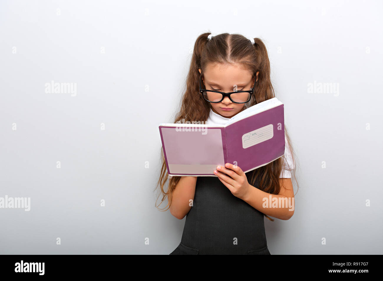 Smart pupil kid girl in eyeglasses looking in the textbook and dooing ...
