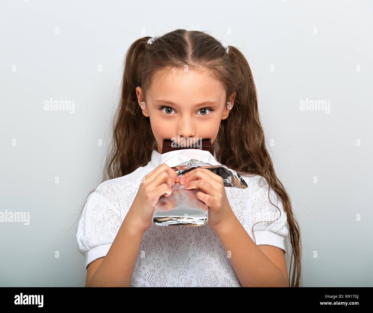 Happy fun smiling kid girl biting dark chocolate with craving eyes ...