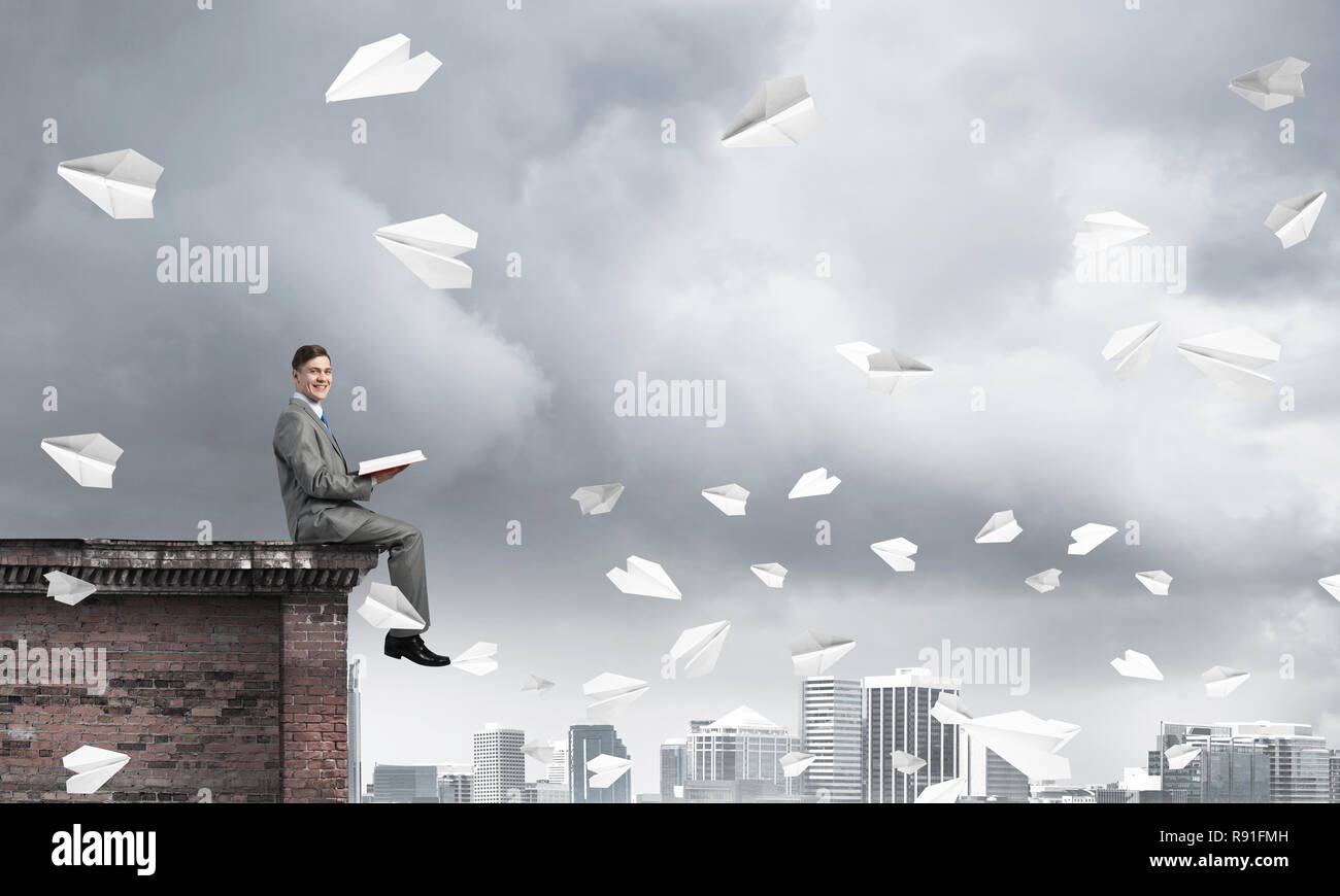 Man on roof edge reading book and cityscape at background Stock Photo ...