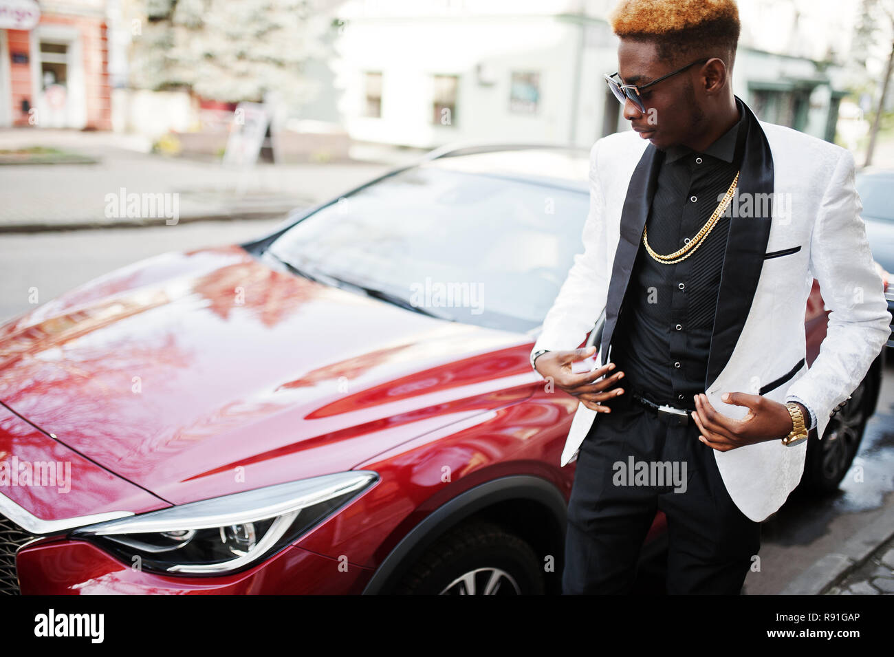 Chic handsome african american man in white suit against red luxury car ...